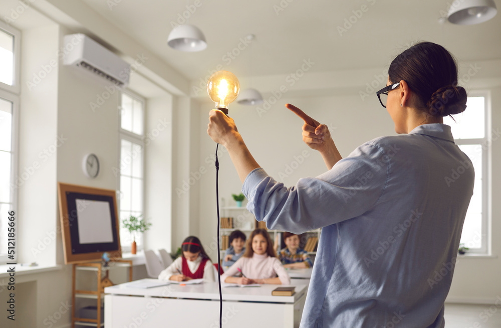 School science teacher shows students shining light bulb. Female ...