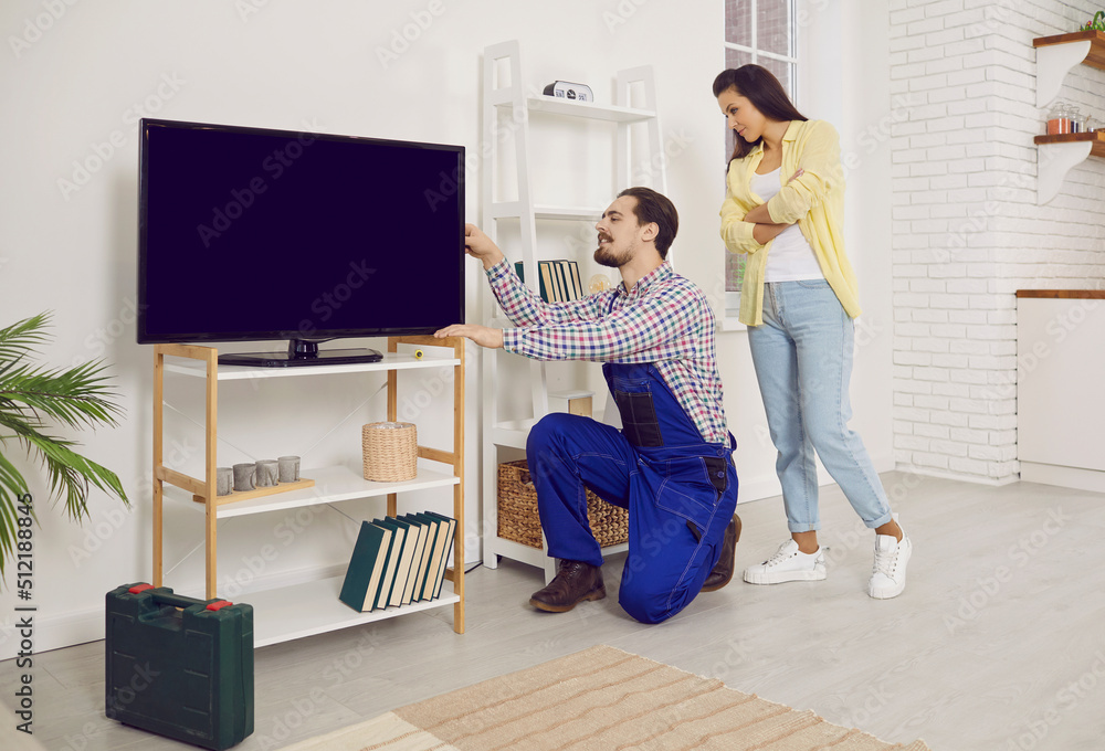 Professional workman in workwear installing large TV monitor in house ...