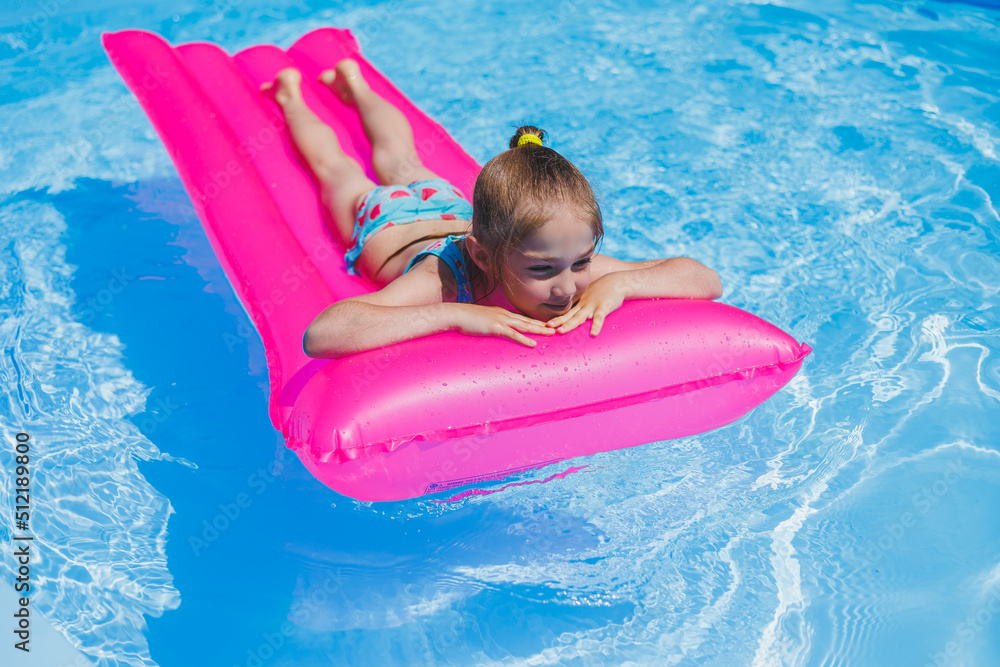 Girl 7-8 years old swims in the pool on an inflatable pink mattress ...