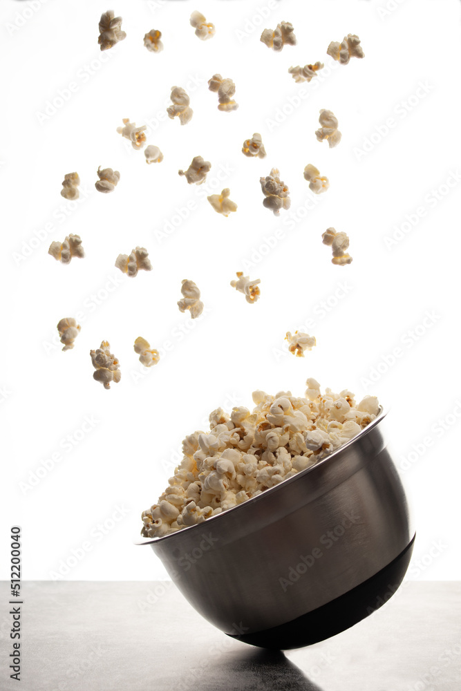 vertical photo of a tilted aluminium bowl filled with popcorn and ...