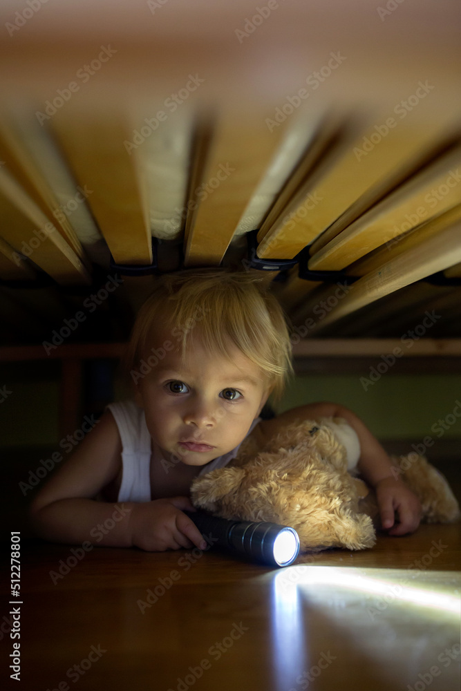 Little child, hiding under the bed, hugging teddy bear and holding ...