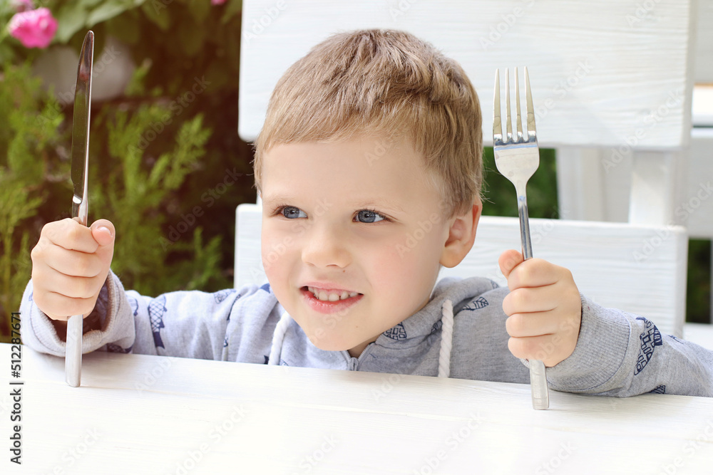The smiling child shows that he wants to eat. Kid holding fork and ...