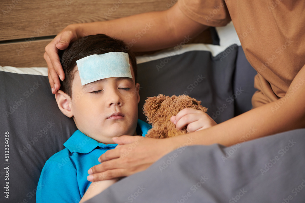 Sick child hugging teddy bear when sleeping in bed with cooling patch ...