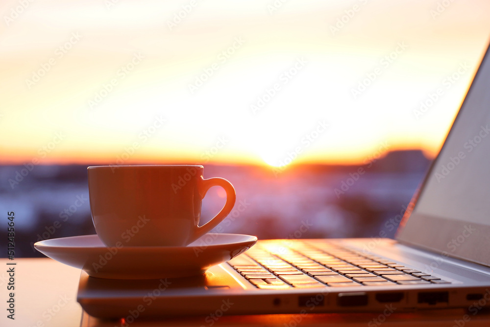 Coffee or tea cup on laptop against the window in sunshine. Cozy ...