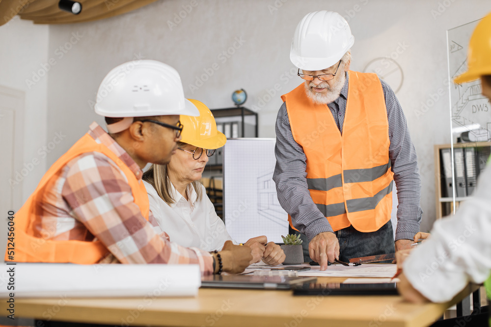 Multiracial architect people in helmets sitting at table with ...
