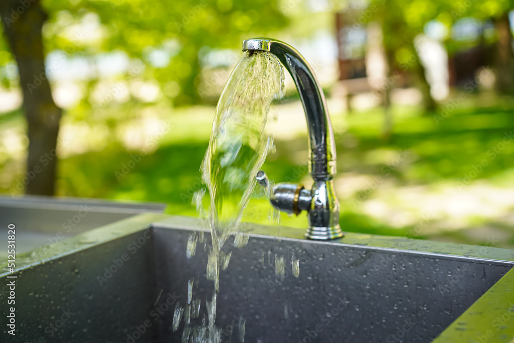 Open faucet with flowing water in nature. Green lawn in the country ...