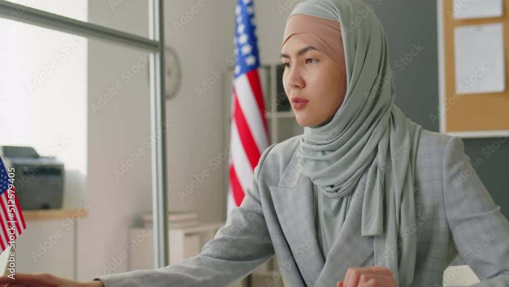 Tilt up shot of young muslim woman in hijab using laptop and checking ...