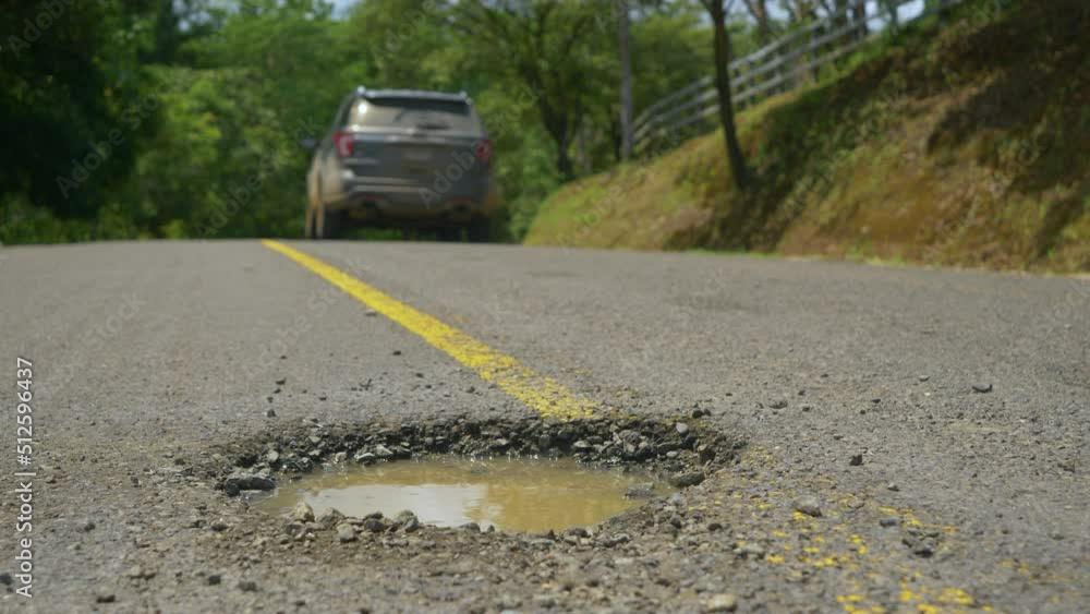 LOW ANGLE, CLOSE UP, DOF: 4x4 vehicle evades a big hole in the road ...
