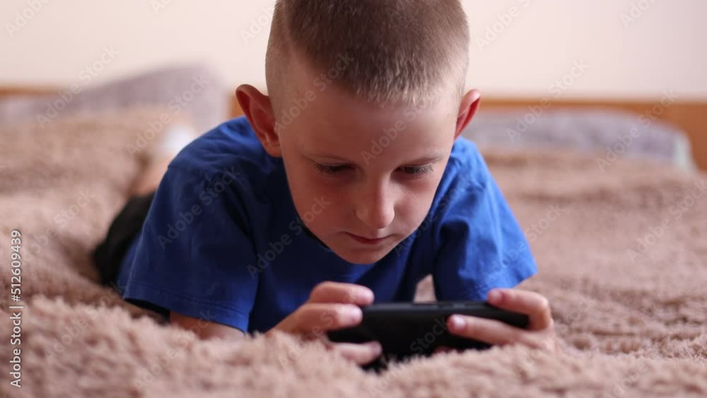 Child's dependence on a mobile device theme. Child is lying on bed and ...