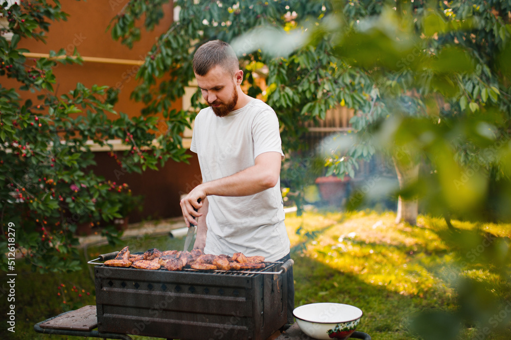 A young man in a white t-shirt with a beard makes a barbecue on the ...