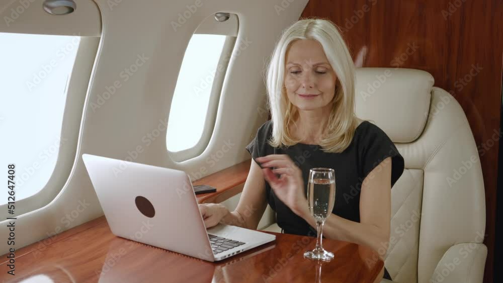 Successful mature women millionaire in airplane working at laptop and ...
