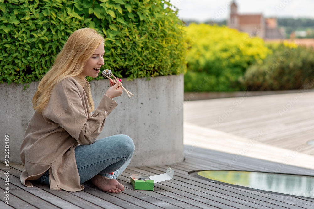 Young beautiful blond woman eating sushi outdoors, on the wooden ...