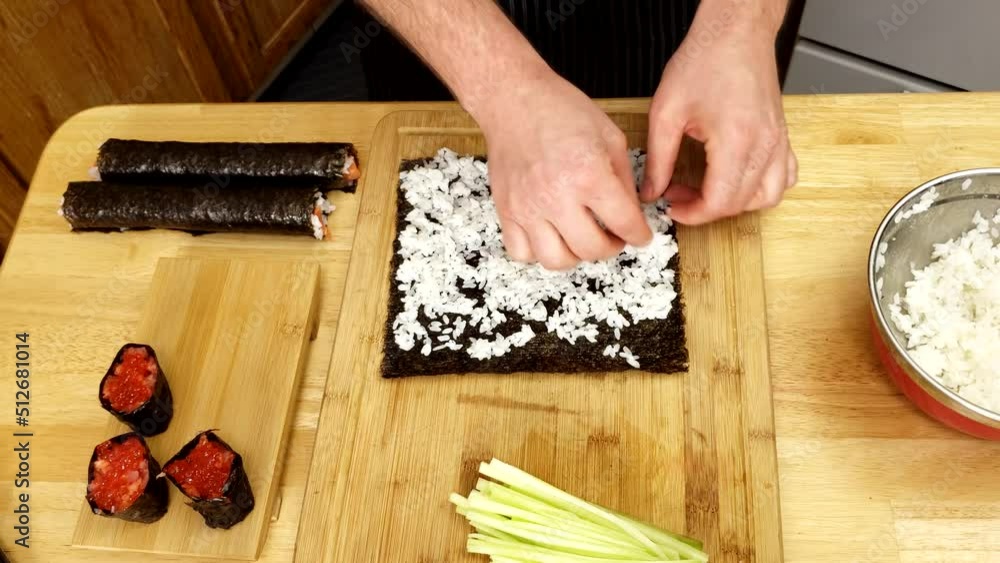Spreading cooked rice onto edible sheet of sea weed and placing pieces ...