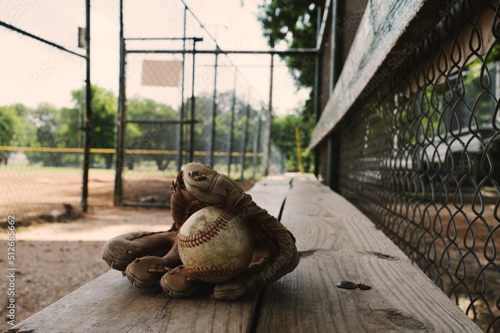 Baseball equipment shows ball and glove on dugout bench at park field ...