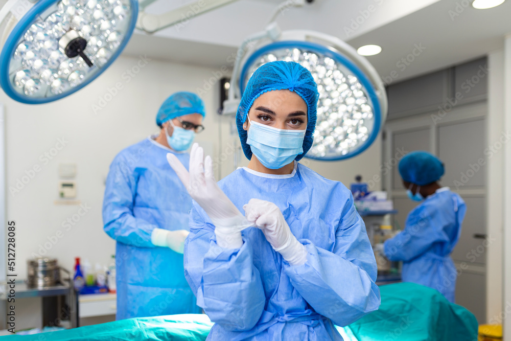 Portrait of beautiful female doctor surgeon putting on medical gloves ...