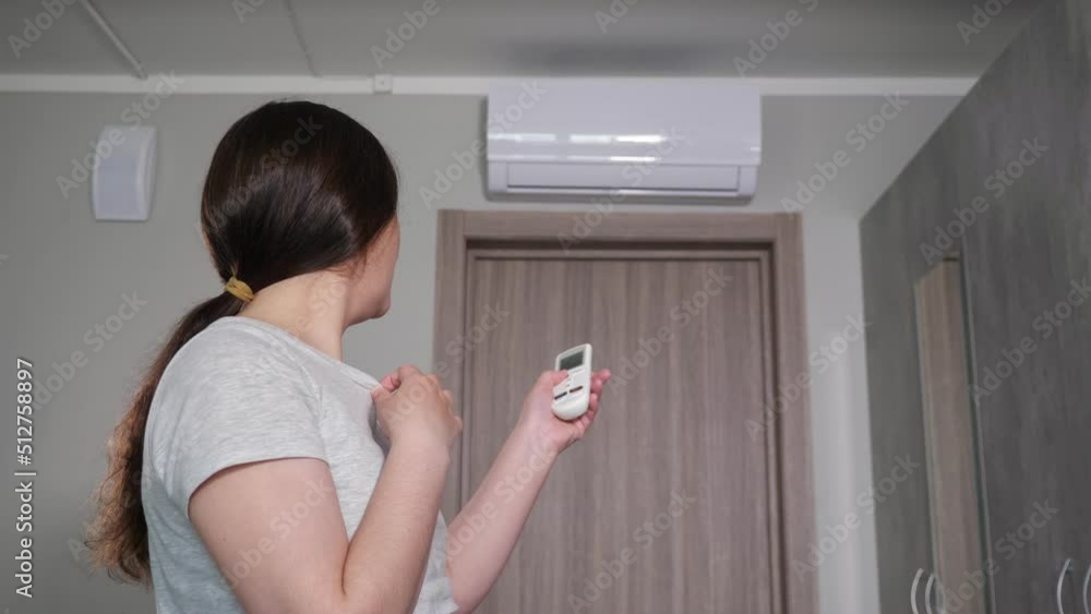 Woman sweats and turns on air conditioner with remote control in hot ...