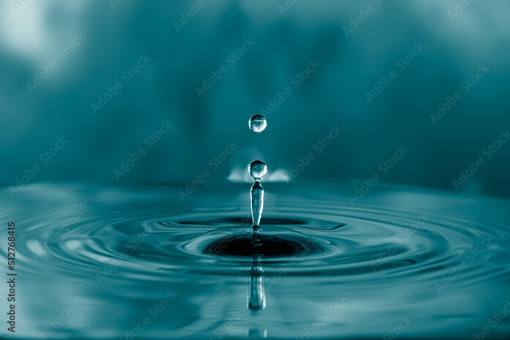 Blue water droplet hits the water surface creating a beautiful pattern ...