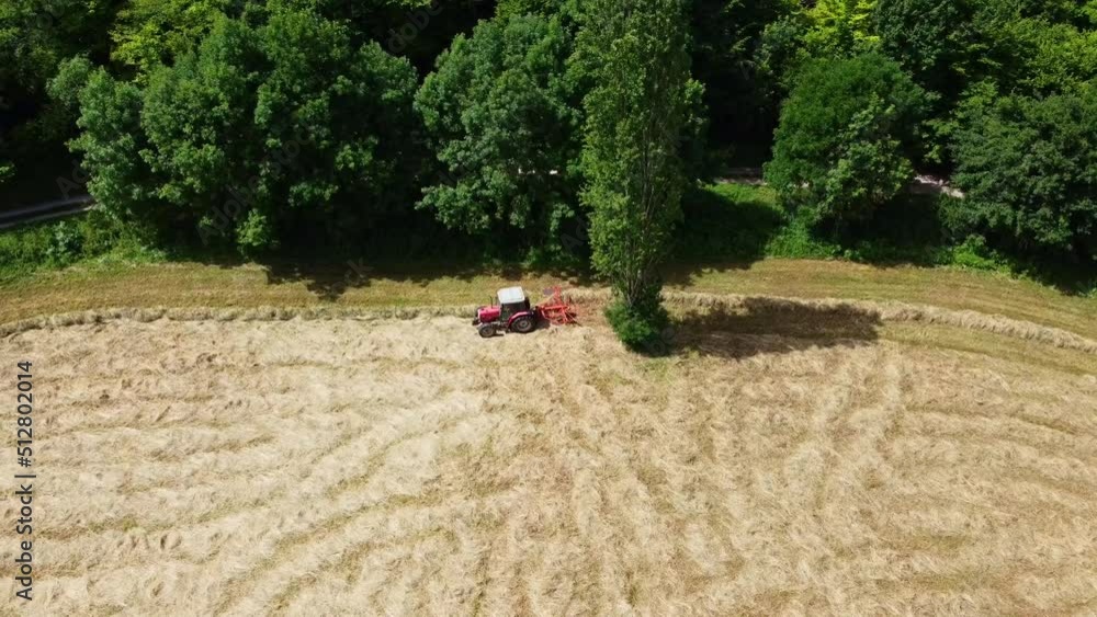 Tracteur vu de profil en train de faire l'andain grâce à une petite ...
