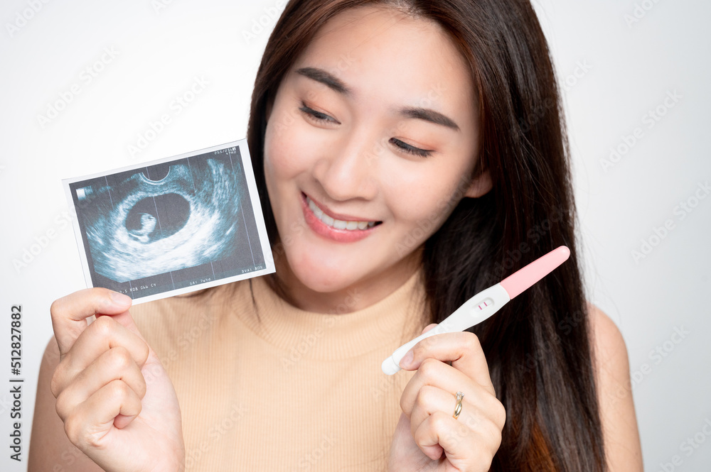 Asian woman holding ultrasound scan and pregnancy test showing a ...