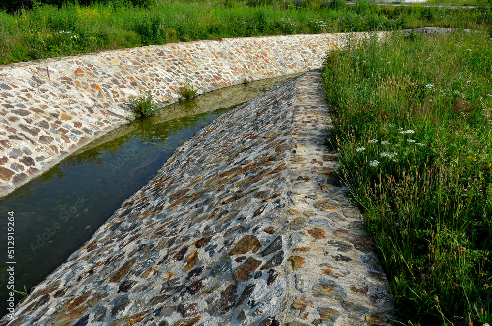 stone lining of bank at the mouth of the sewer pipe with a grate ...