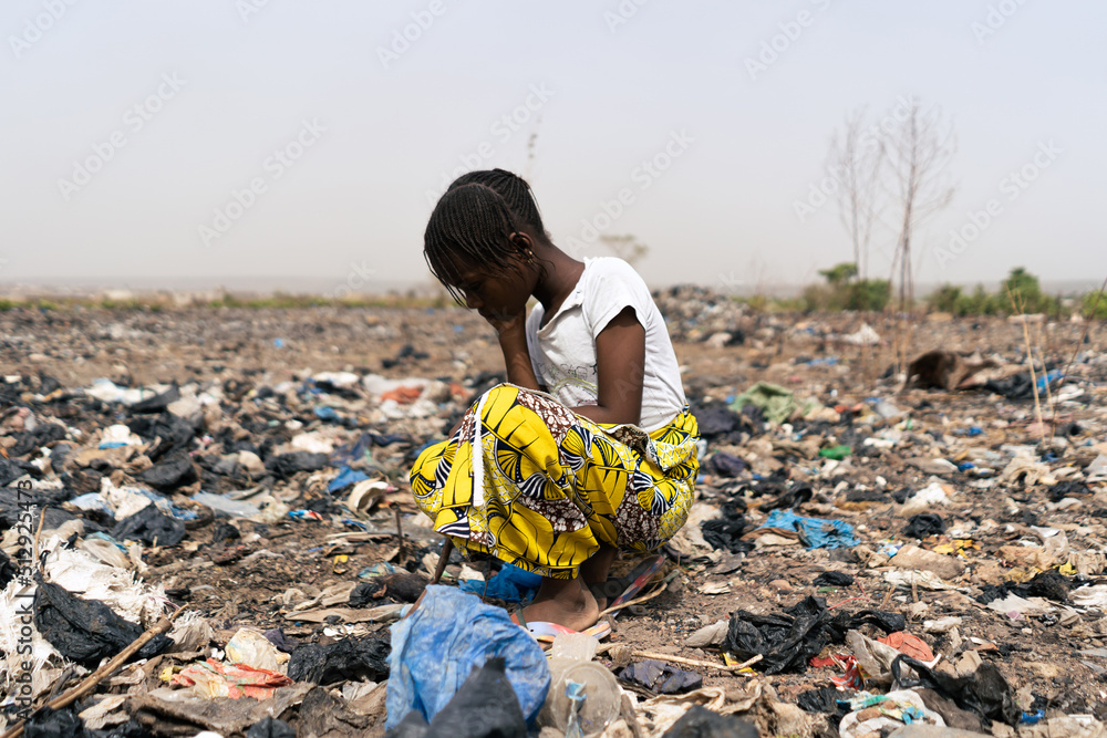 Tired little African girl who is desperately looking in the rubbish ...