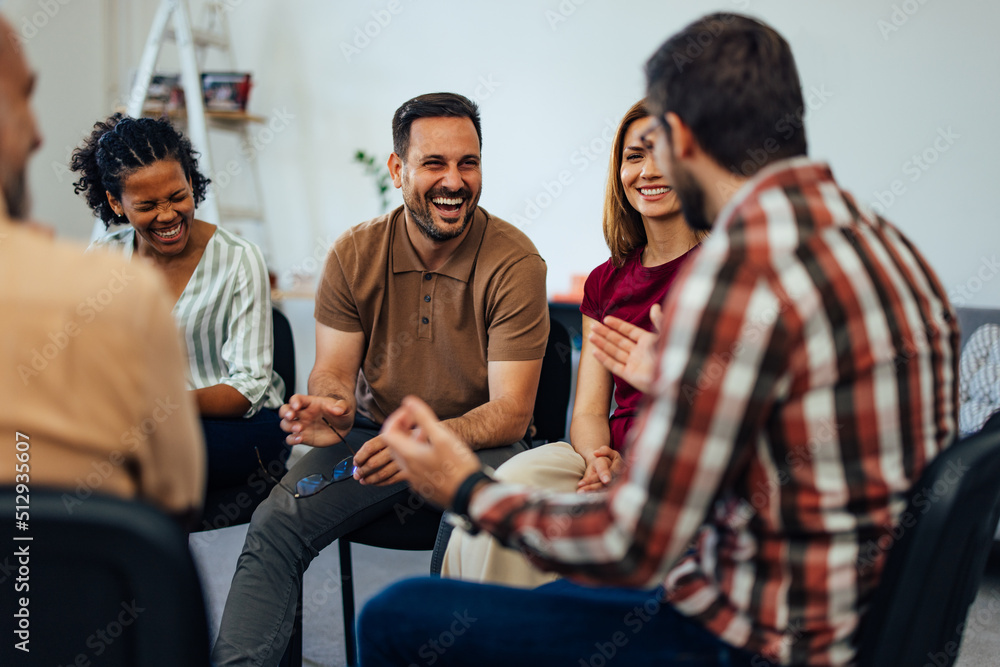 Focus on the smiling people, sitting around each other, at the group ...