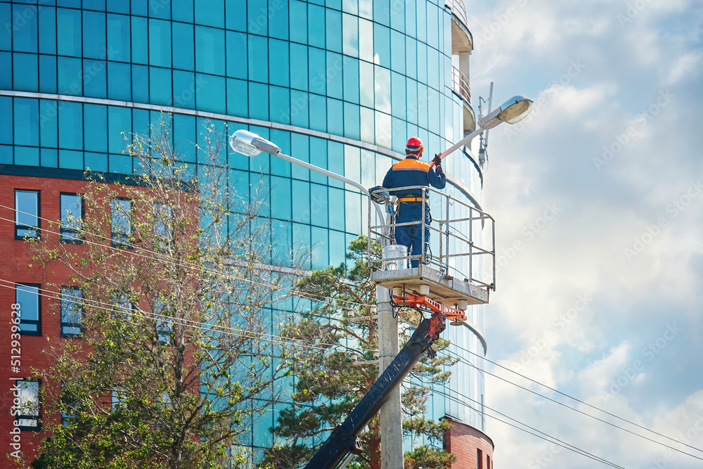 Man in cradle painting lamppost. Worker in aerial platform, man paint ...