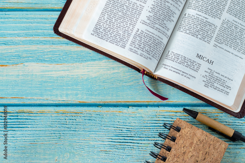 Micah open Holy Bible Book on a rustic wooden table background with a notebook and pen. Copy ...