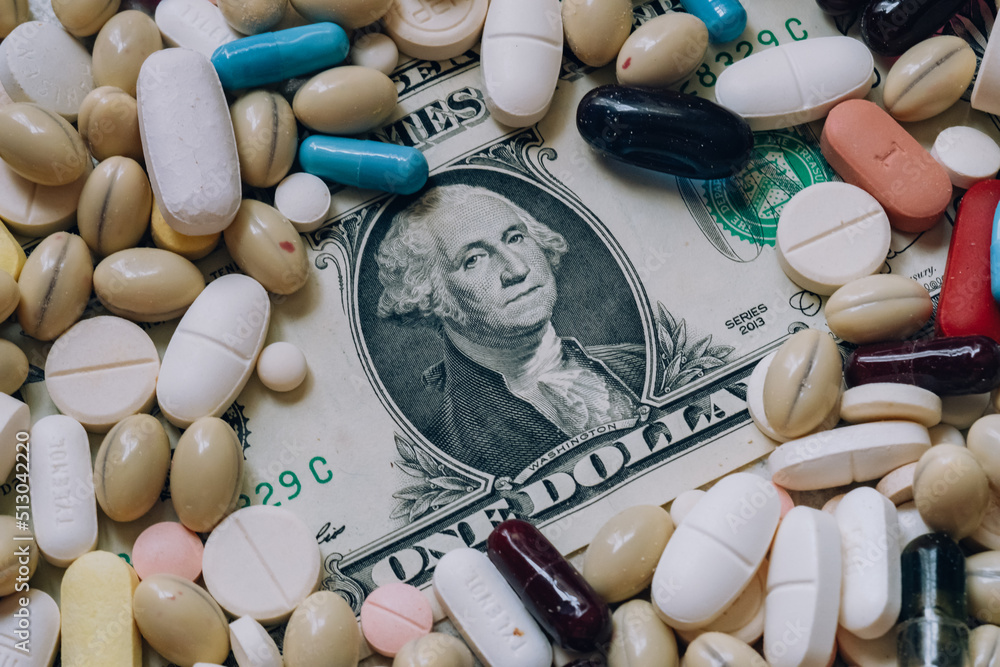 Photo of a US one dollar bill among pills of many shapes and colors ...