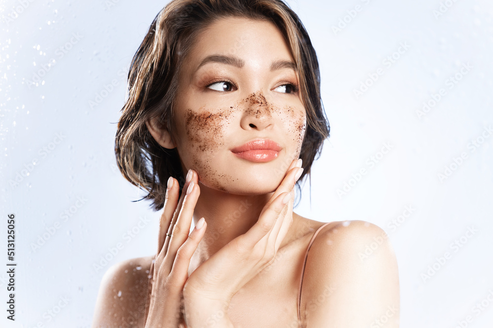 Beautiful young girl with naked shoulders scrubbing face, pretty female cleansing facial skin by ...