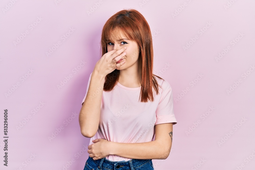 Redhead young woman wearing casual pink t shirt smelling something ...