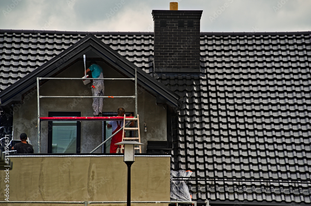 Applying facade plaster on the walls of a newly built house. People at ...