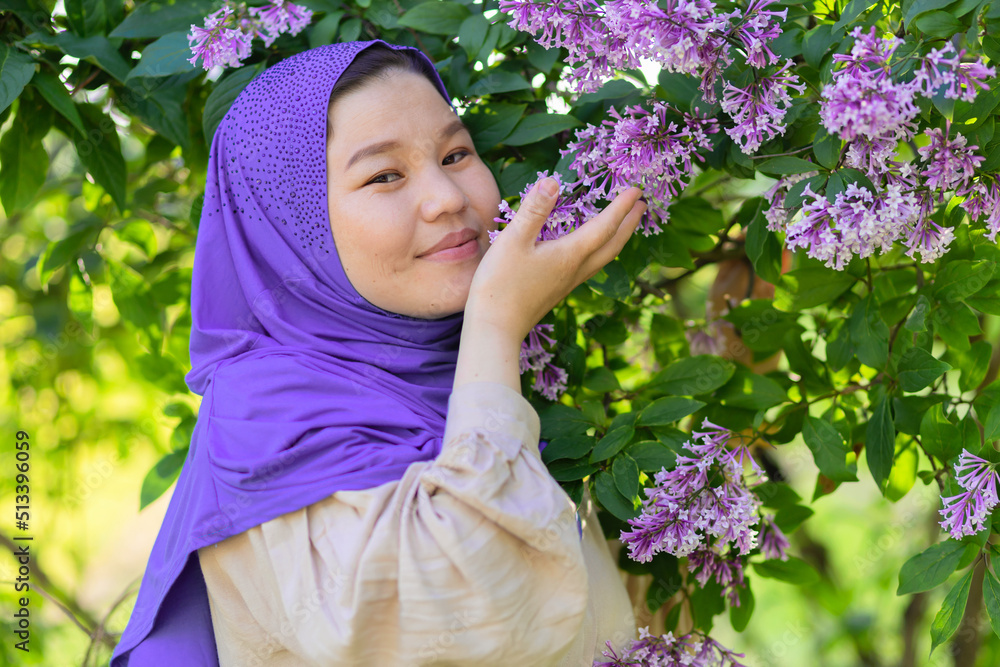 beautiful young asian islamic woman in hijab, headscarf sniffing lilac ...