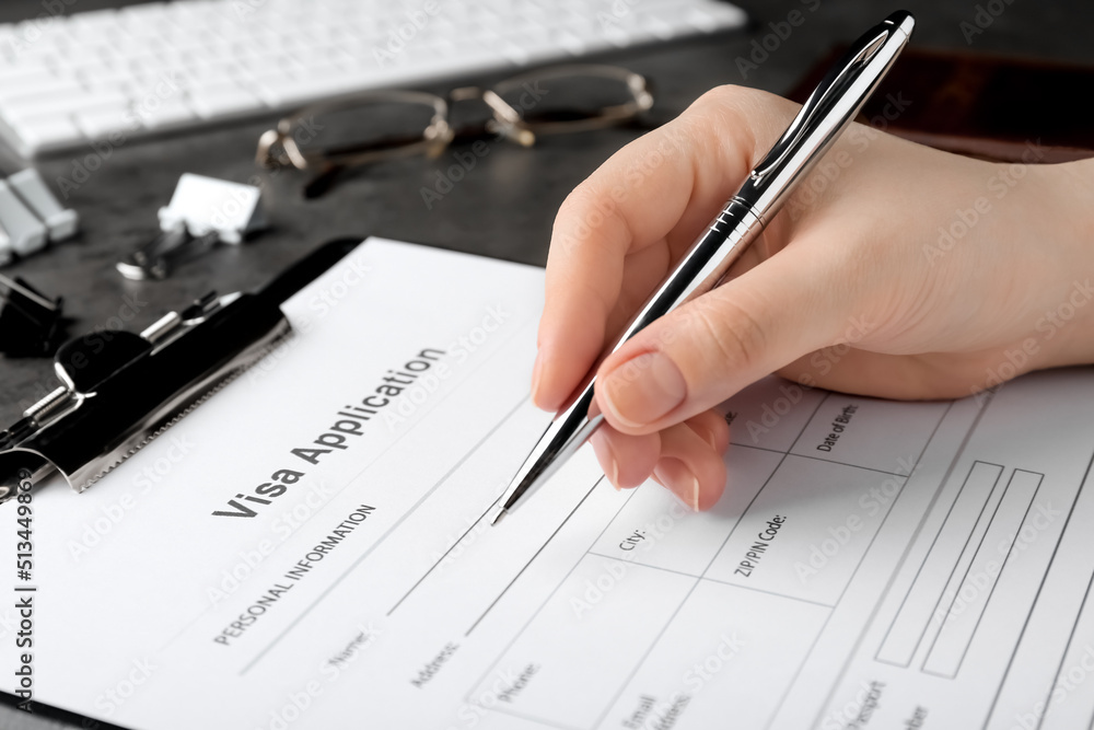 Woman filling visa application form for immigration at grey table ...