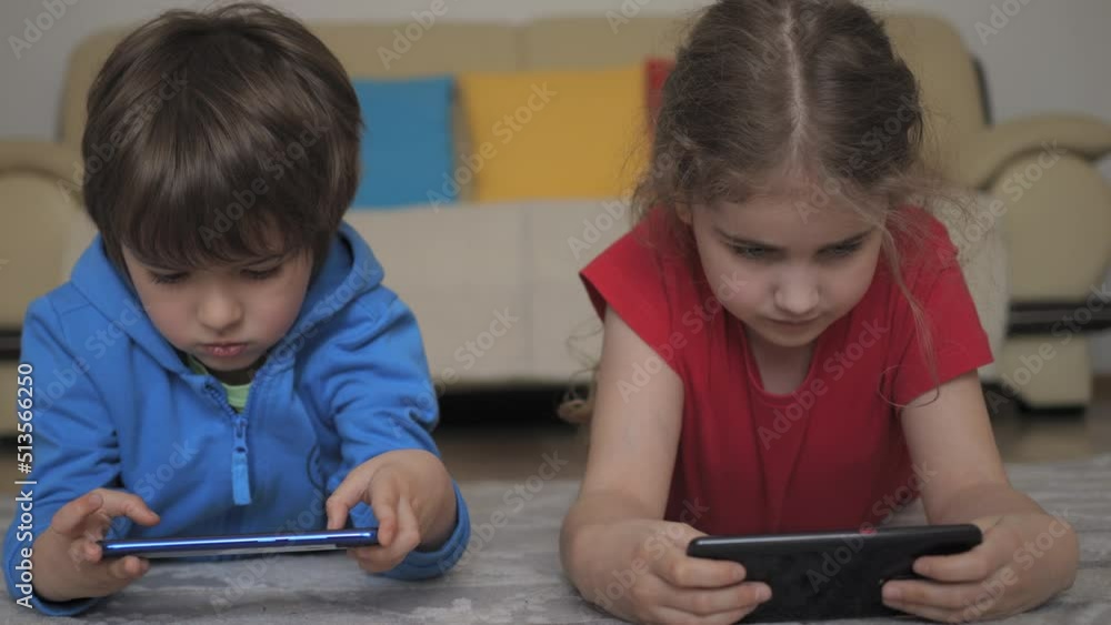 Children Playing Games In Phone at Home Lying on Floor. Kids Playing Video Game on Mobile Phone ...
