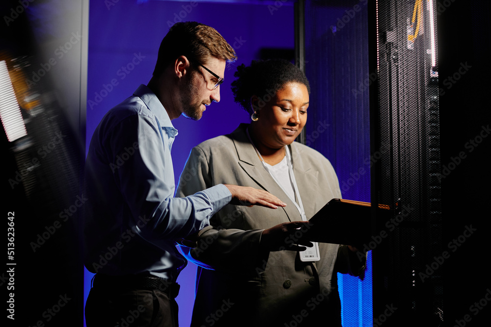 Waist up portrait of two system administrators using computer in dark ...