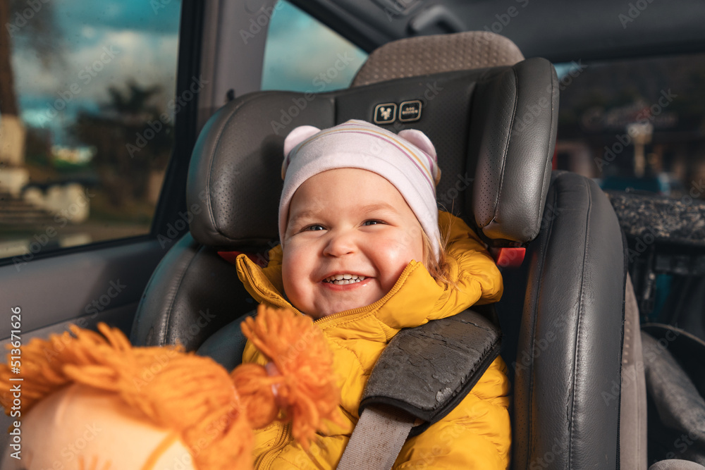 Portrait of a happy little kid sitting in a child seat in the back seat ...