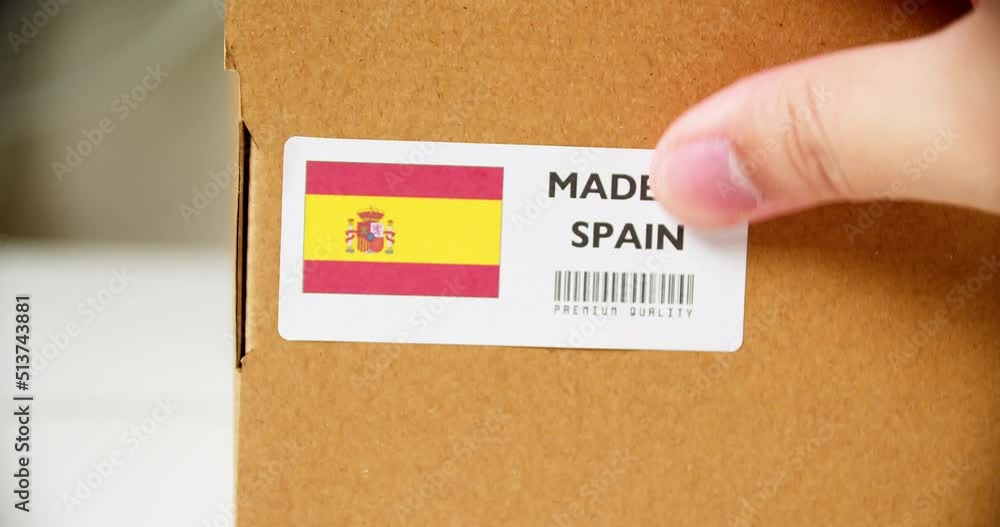 Hands applying MADE IN SPAIN flag label on a shipping cardboard box ...