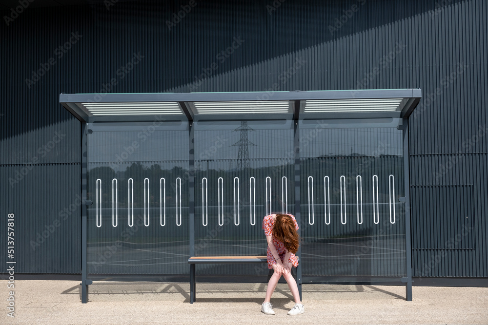 Sad young woman sitting alone at bus stop Stock Photo | Adobe Stock