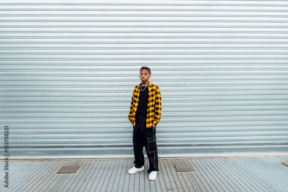 Young man standing with hands in pockets in front of shutter Stock ...