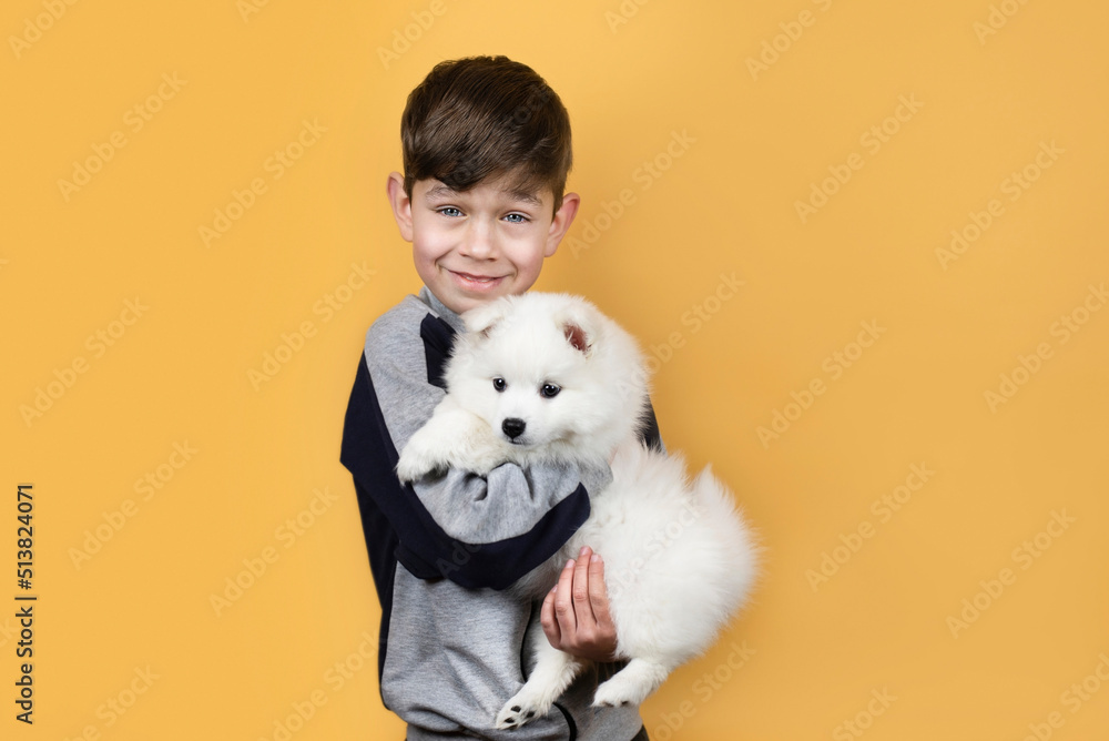 Handsome young boy happily holds his little white dog in his arms and ...