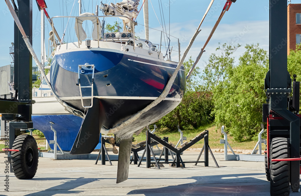 Blue sloop rigged sailboat lifted by a crane being placed back in the ...