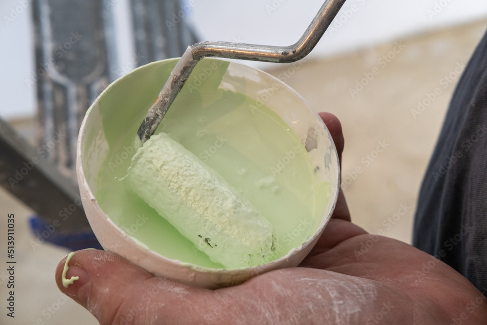 Craftsman's hand holding a roller in a can of green paint. Painter ...