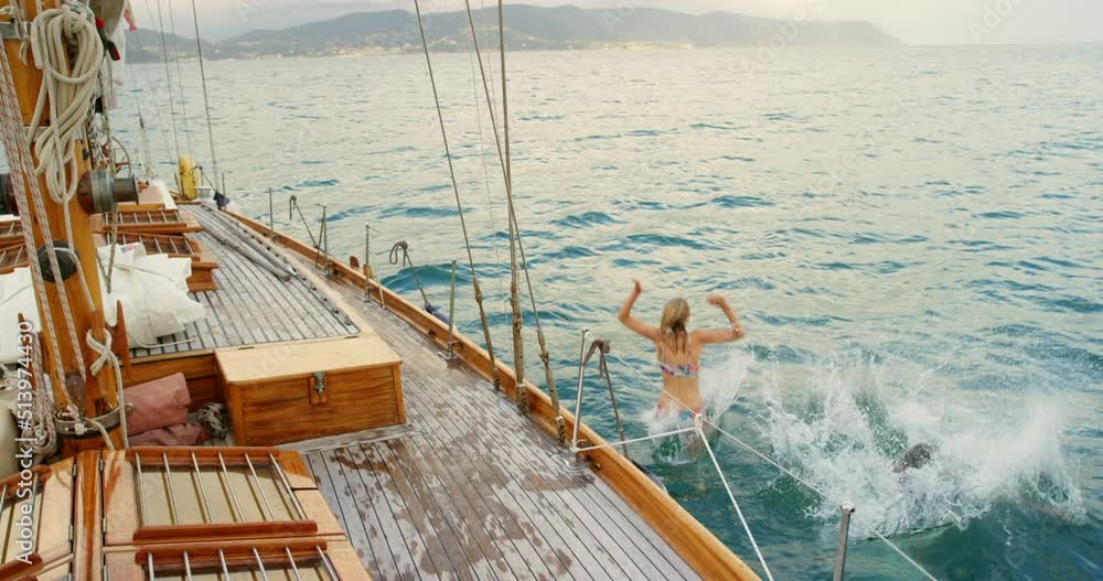 Carefree women in bikinis jumping off a boat into the ocean to swim ...