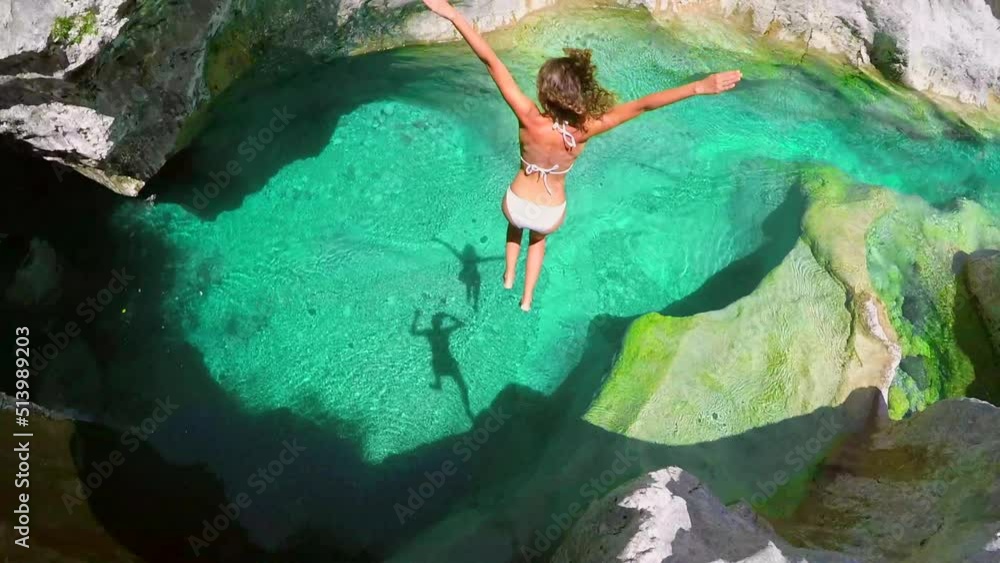 Happy young woman in white bikini jumping from cliff swimming in a lake ...