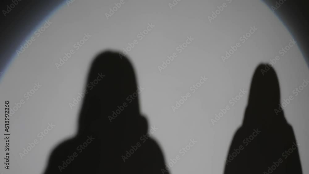 Two female shadows come out into the light from the spotlight and turn ...