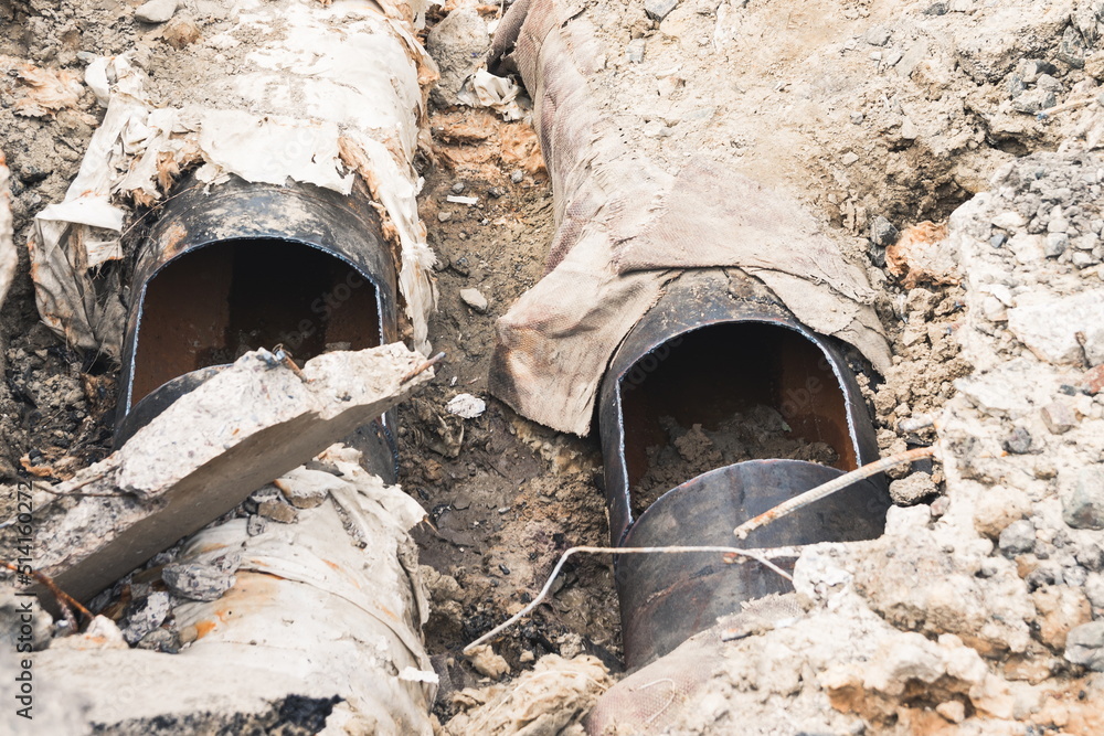 Old broken pipes dug up on the road in the city. Water flows from an ...