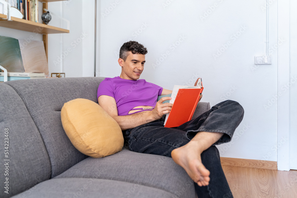 Transgender Man Reading Book Sitting On Armchair Stock Photo | Adobe Stock