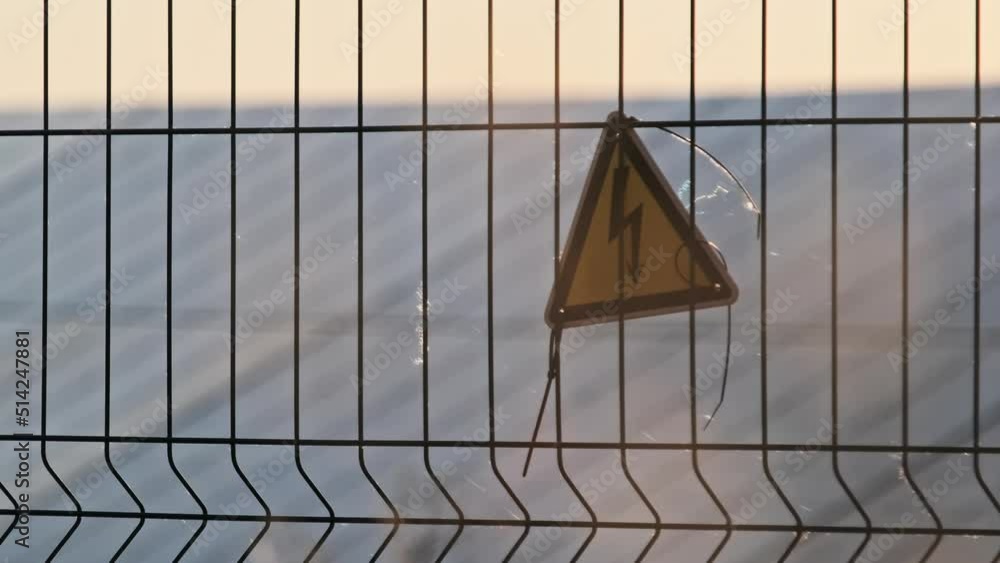 High voltage sign on a wire fence of the solar plant. Yellow triangular ...