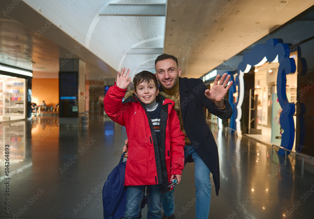Happy family of young dad and his cute boy son waving looking at camera ...